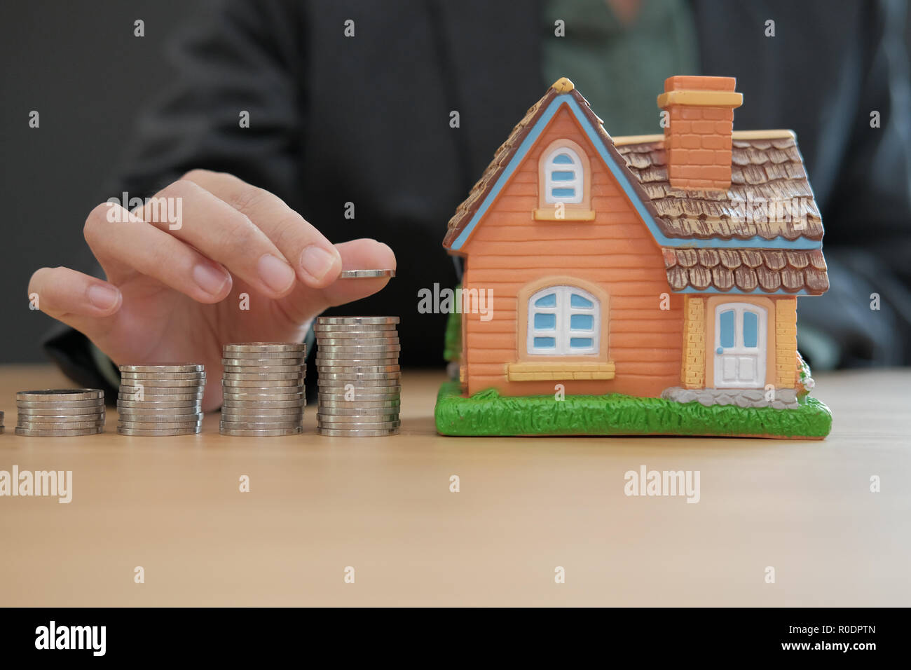 hand putting coins on stack with house model. saving money for buying ...