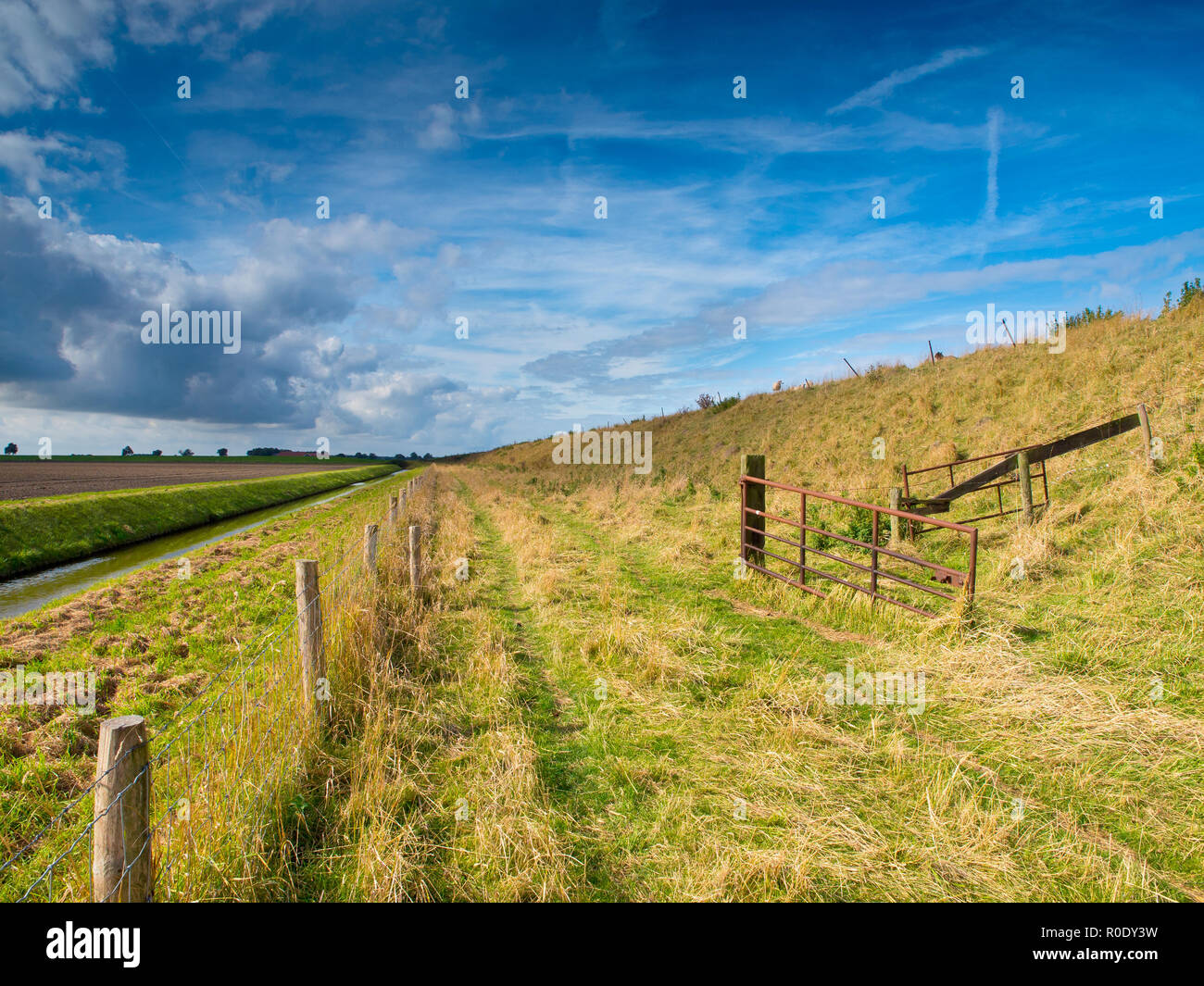 Farm Trail along a Dutch Dike with Gate and Fence under cloudy Summer ...