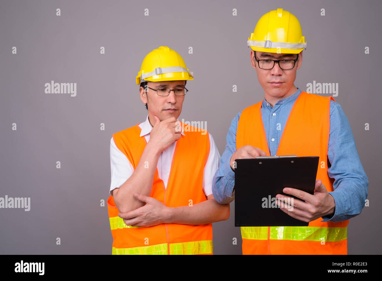 Two young Asian men construction worker together against gray ba Stock ...