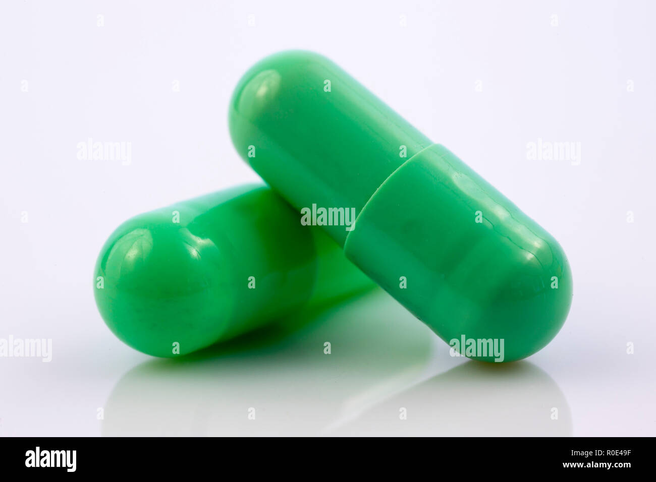 Two green capsules isolated on white reflective background. Global ...
