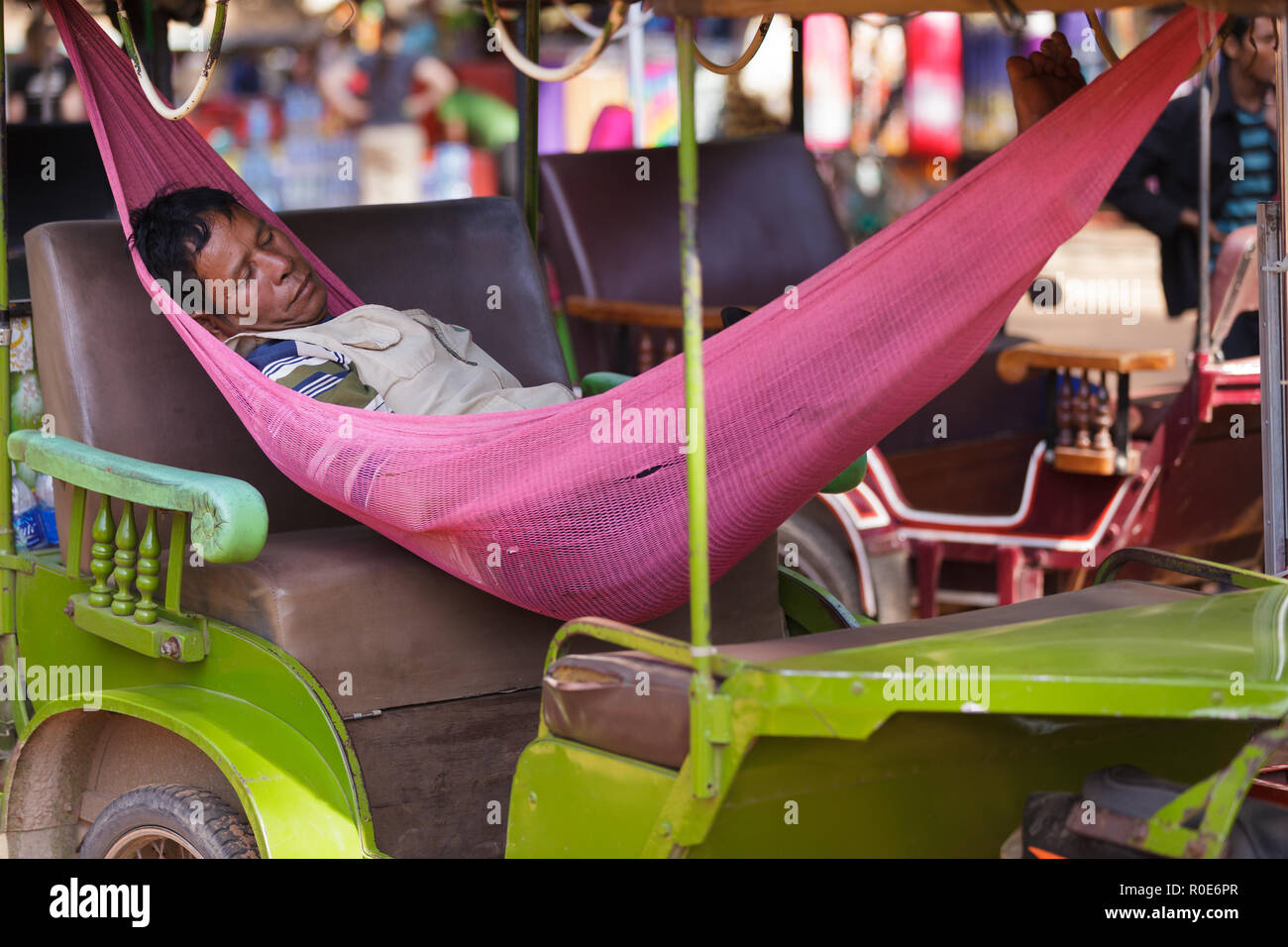 SIEM REAP, CAMBODIA, DECEMBER 3, 2012: A tuk-tuk driver is taking a nap lying in a hammock ...