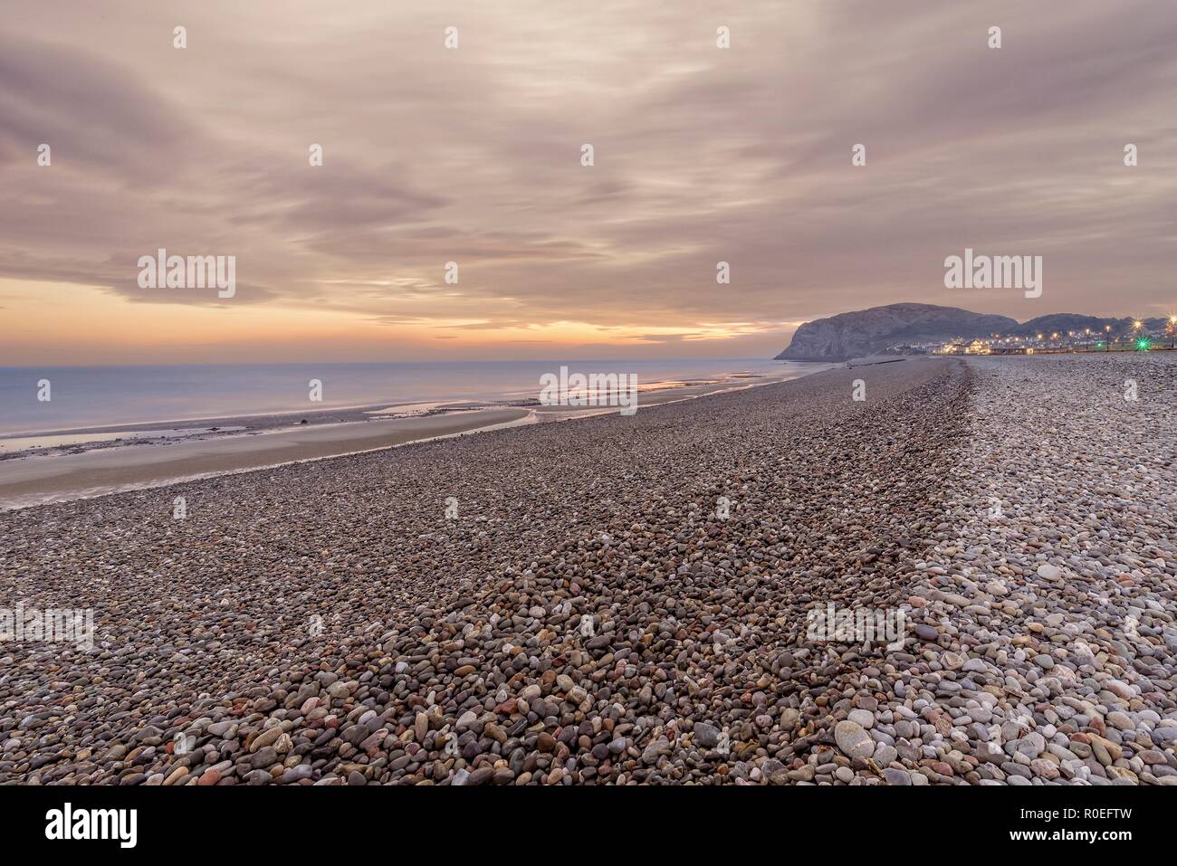 A view of Llandudno’s shoreline at dawn with a red sky and lights along ...