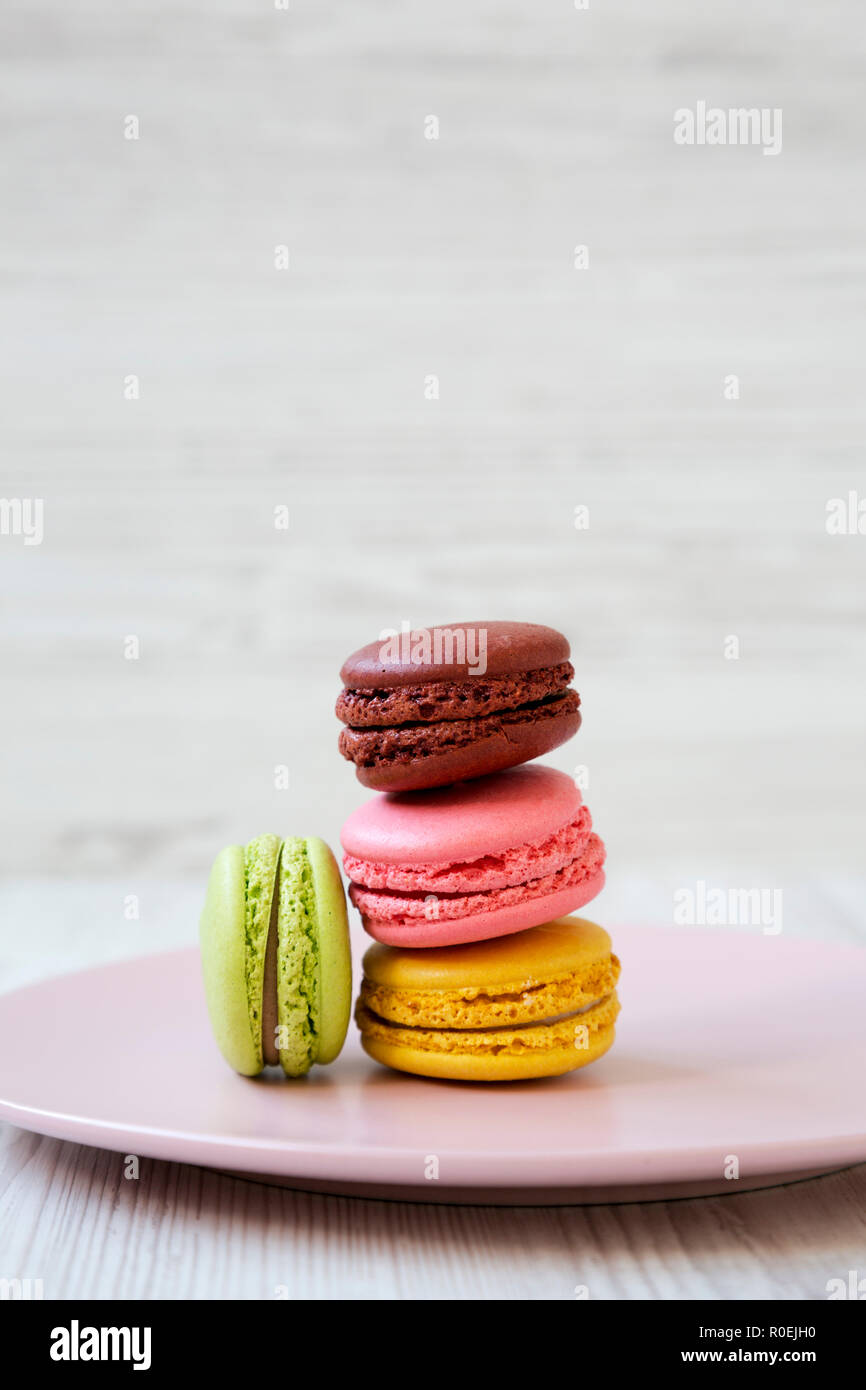 Sweet and colorful macaroons on pink plate on a white wooden background ...