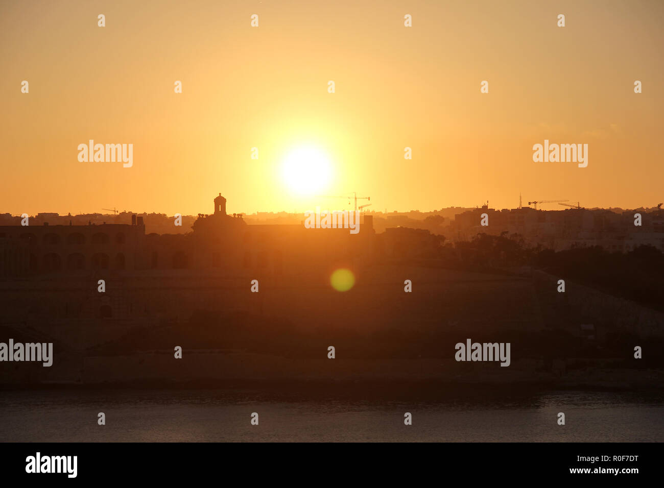 Orange sunset with sun disk above silhouette of city towers and ...