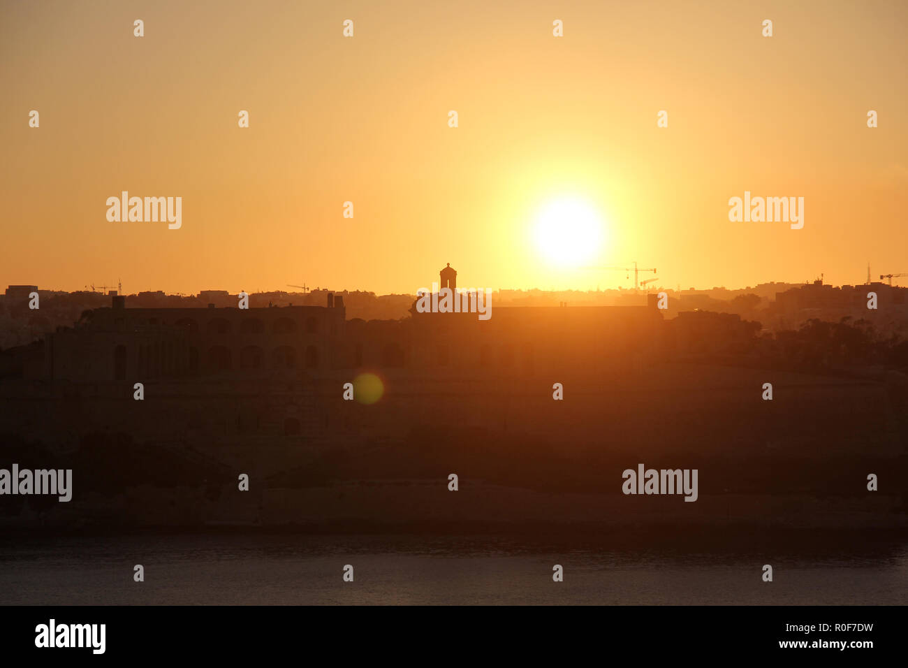 Orange sunset with sun disk above silhouette of city towers and ...