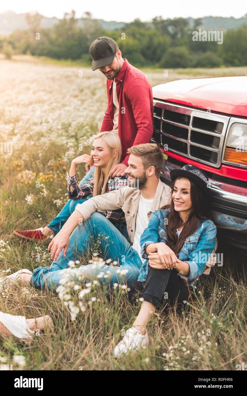 group of young car travellers sitting on flower field and leaning back ...