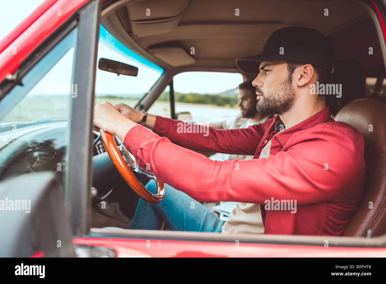 side view of serious young men riding car in field Stock Photo - Alamy
