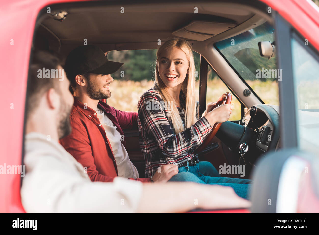 group of happy friends travelling by car and riding by flower field ...