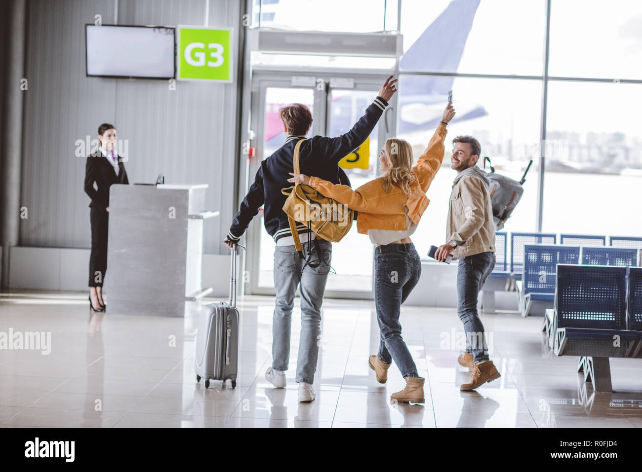 back view of happy young friends waving hands and going to check-in ...