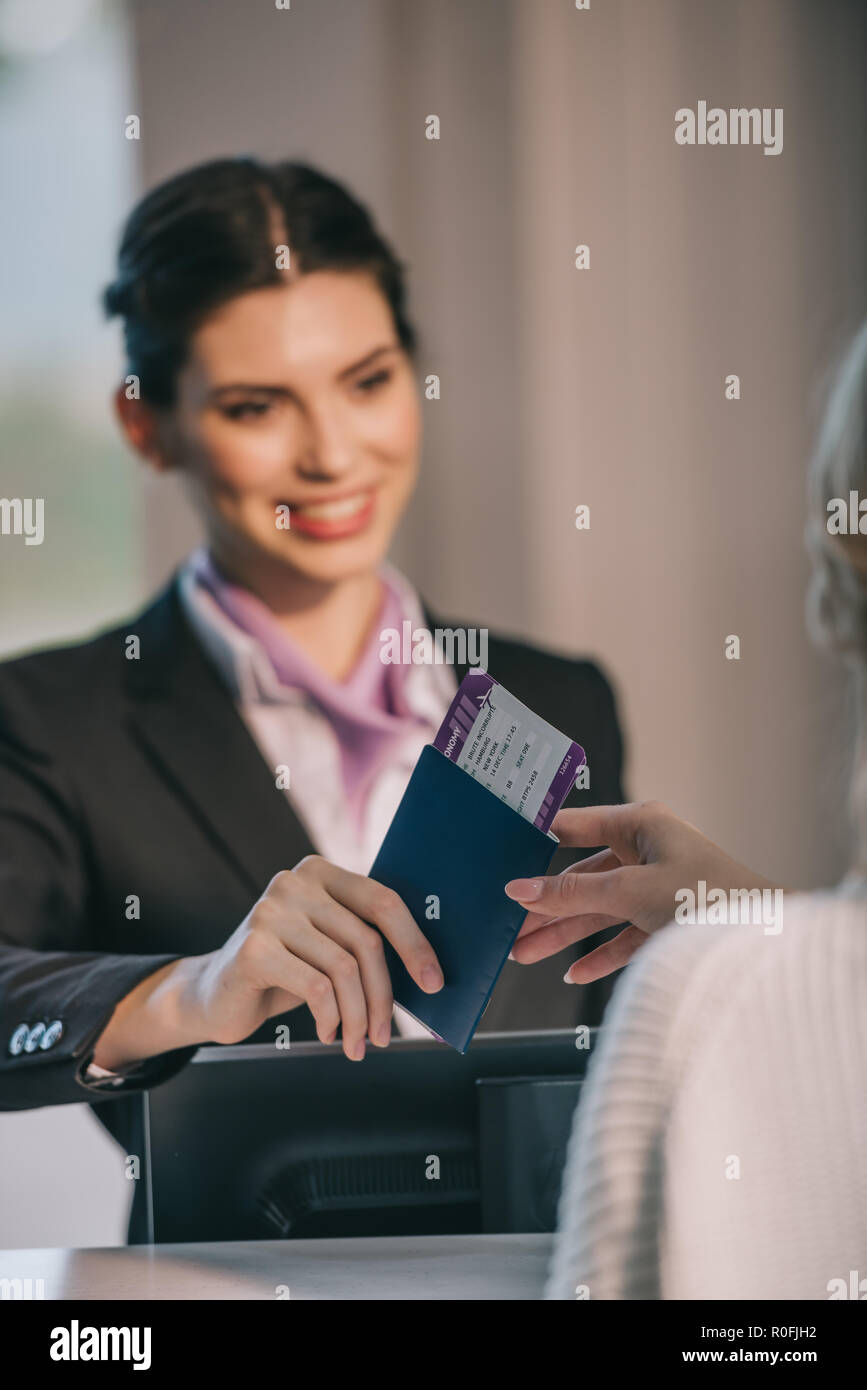 smiling airport worker giving passport with boarding pass to young ...