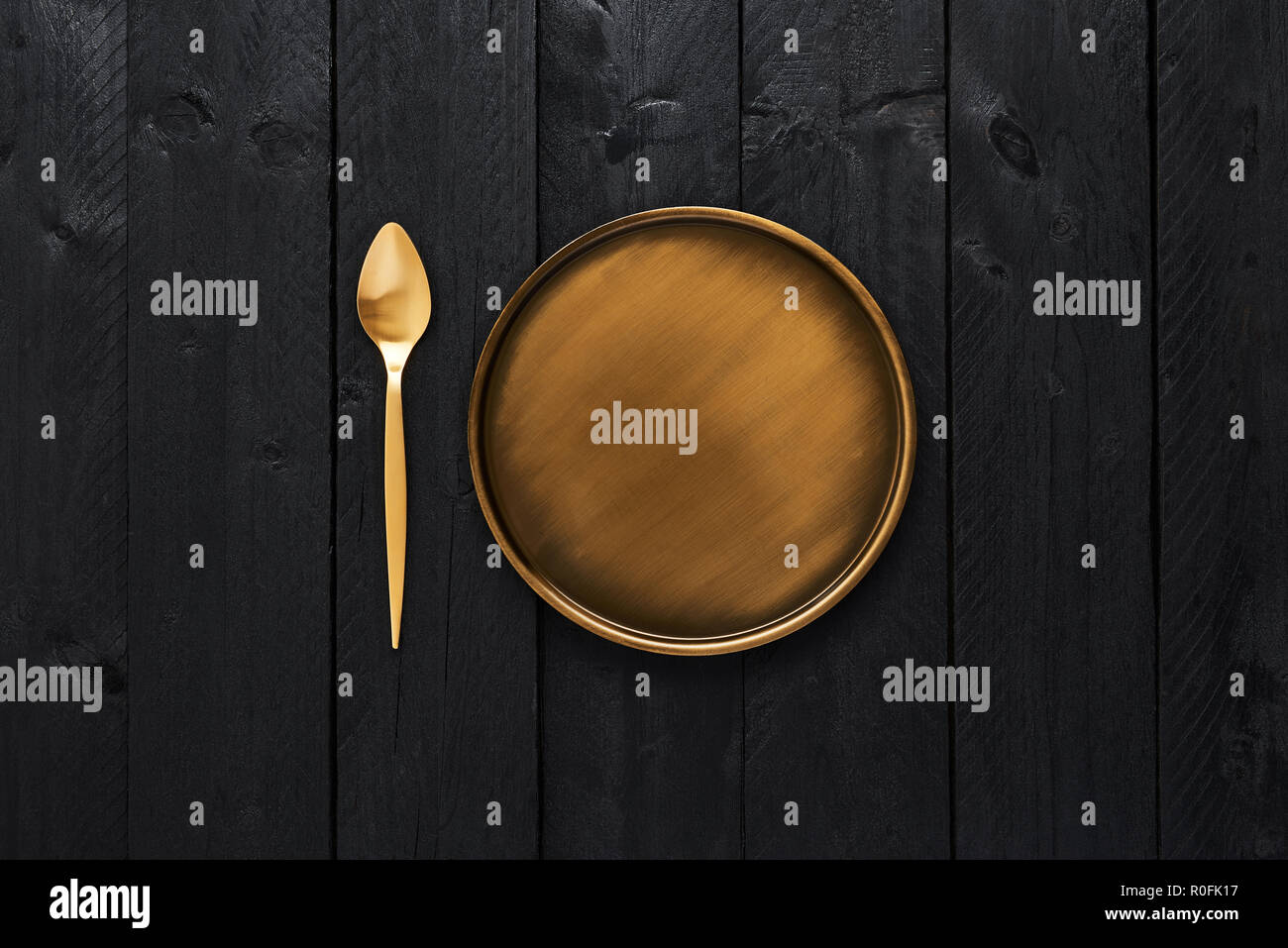 Top view of golden spoon and serving plate on black wooden table with ...