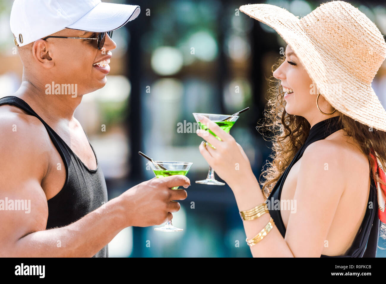 side view of smiling boyfriend and girlfriend standing with cocktails ...