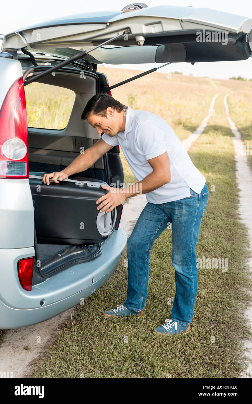 happy man packing suitcase into luggage boot of car in field Stock ...