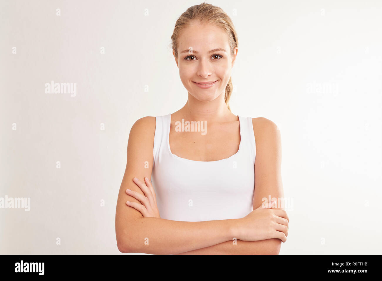 Studio portrait of beautiful smiling young woman standing with arms ...