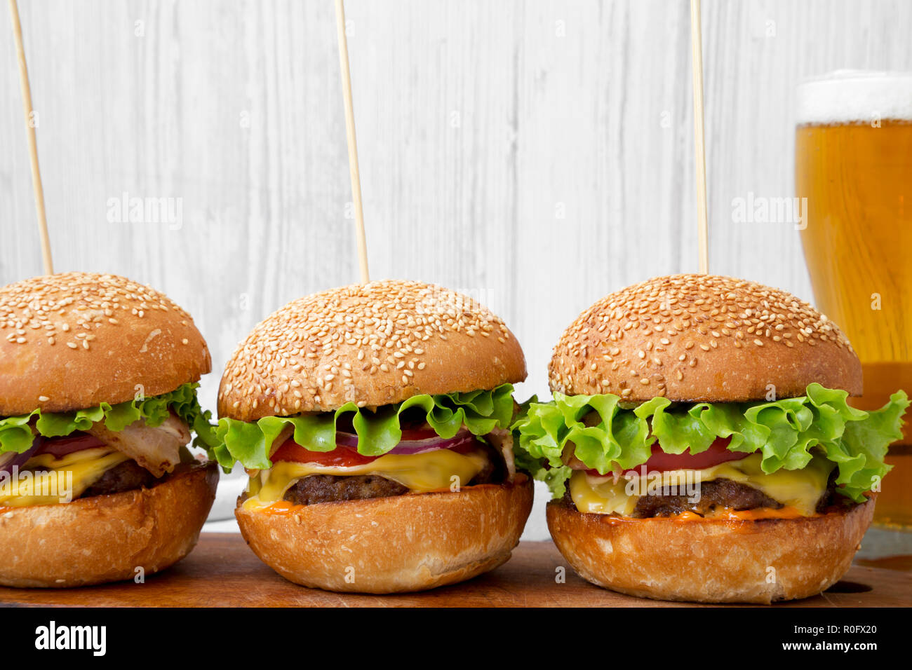 Cheeseburgers and glass of beer on white wooden background, side view ...