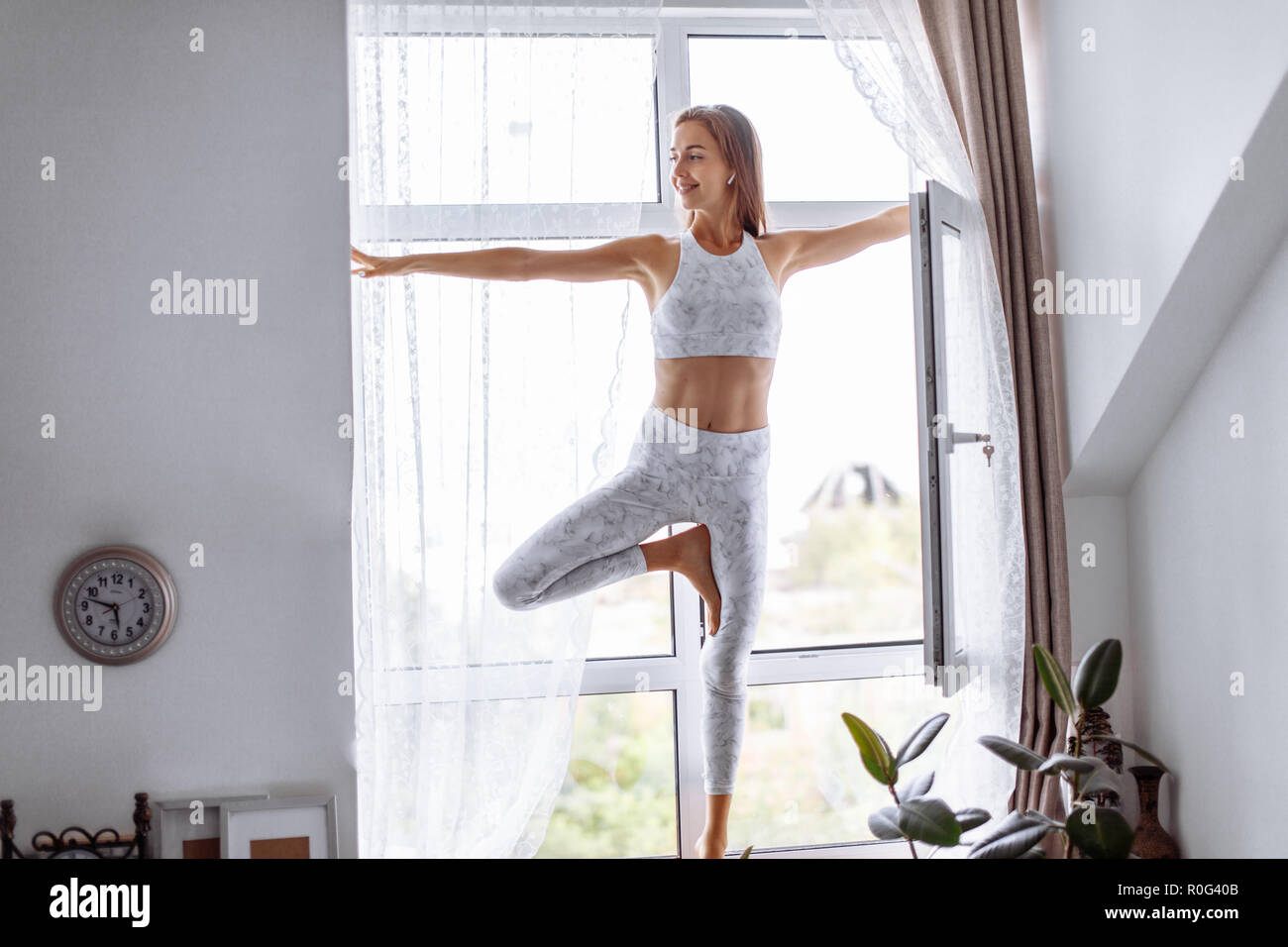 Young skinny flexiable woman doing yoga on one leg against window ...