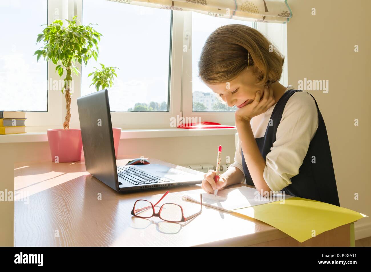 Schoolgirl, girl of 8 years, sitting at table with books and writing in ...