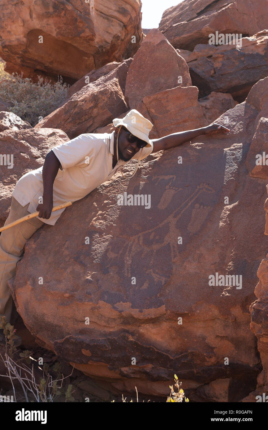 Namibia tourist guide showing tourists ancient bushman rock engravings ...