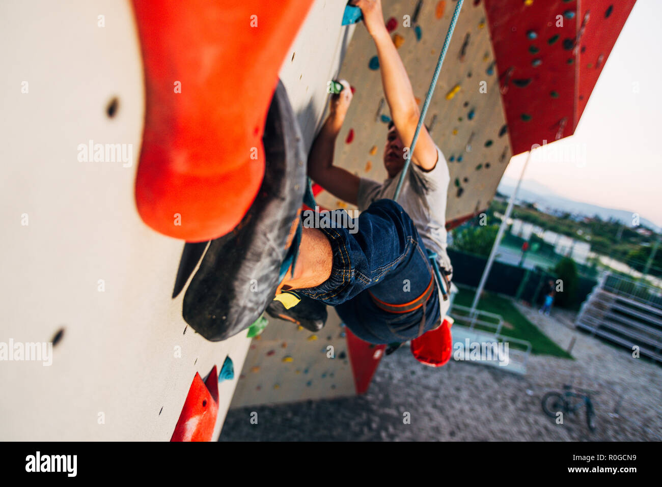 Man wearing belaying rope, climbing on a very high rock climbing wall ...