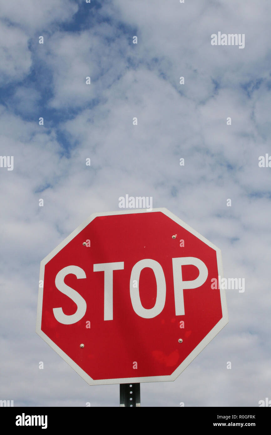 A bright red stop sign high in the blue sky with white clouds ...
