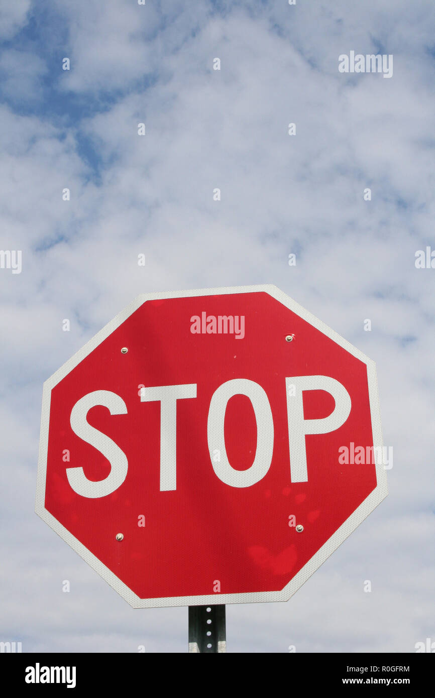 A bright red stop sign high in the blue sky with white clouds ...