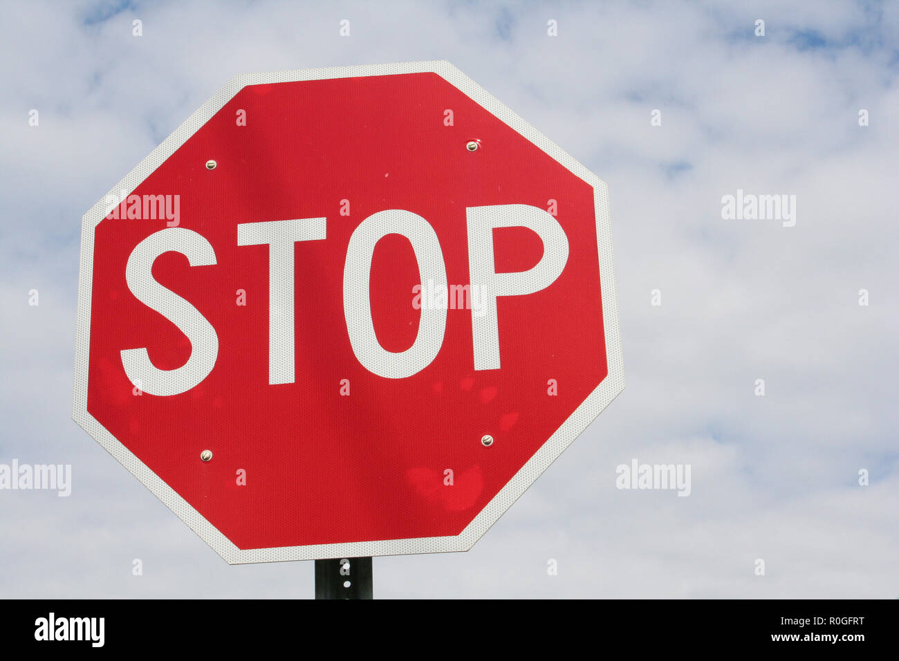 A bright red stop sign high in the blue sky with white clouds ...