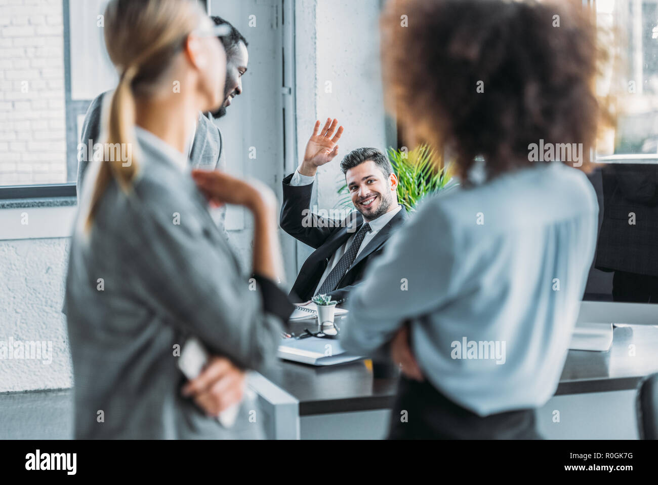 smiling businessman waving hand to multicultural colleagues in office ...