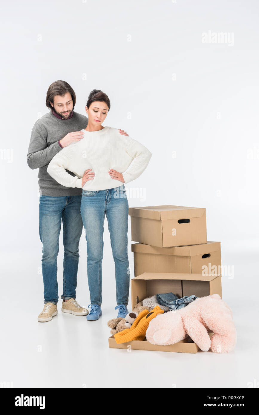 husband hugging thoughtful wife looking at carton box with toys ...