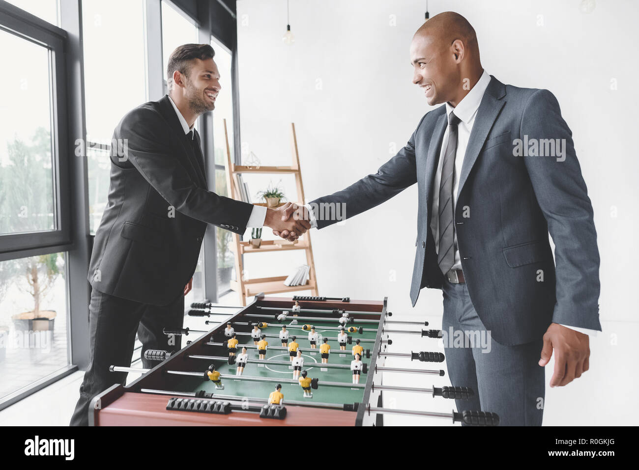 side view of smiling businessmen shaking hands after playing table ...