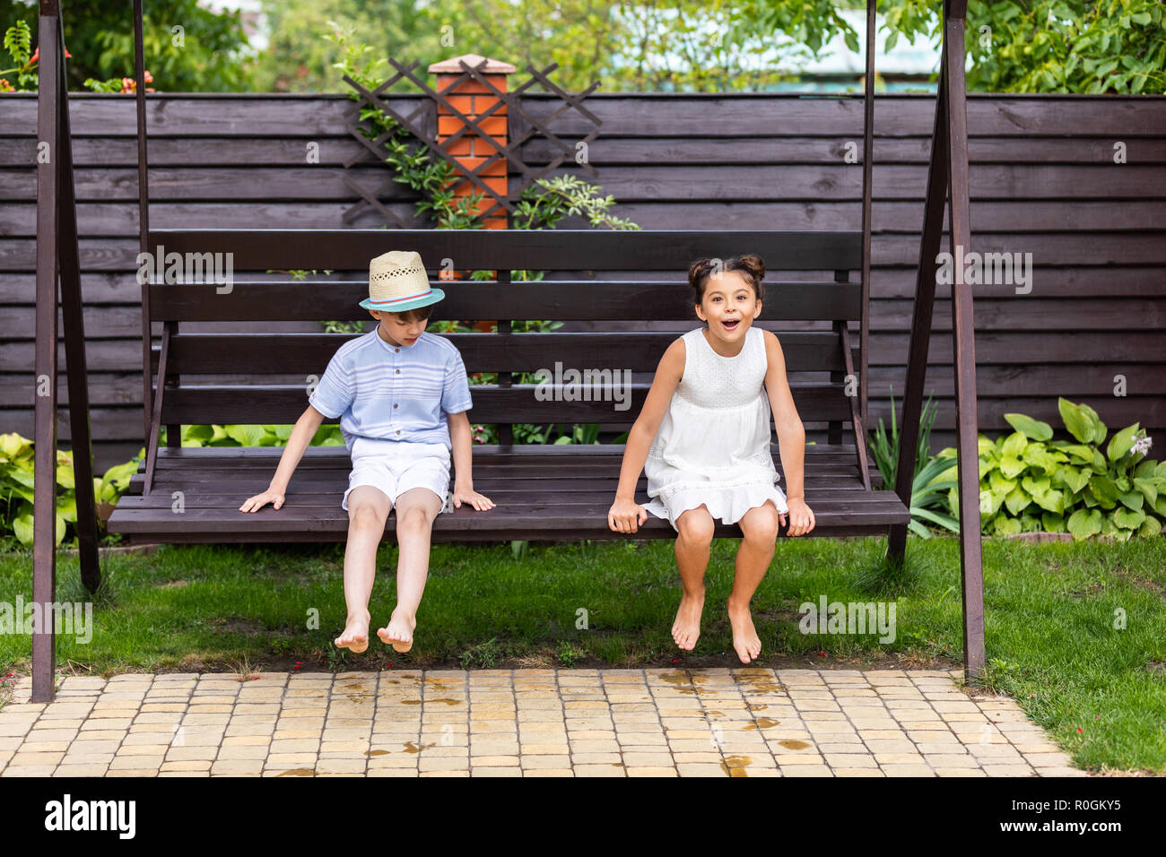 cute kids sitting on wooden bench together on backyard on summer day ...