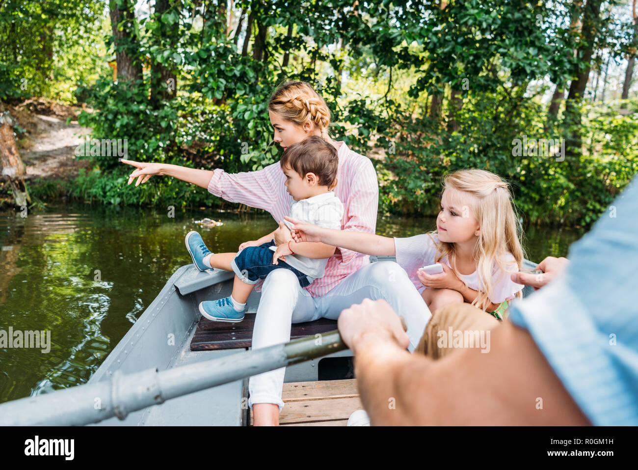 beautiful young family riding boat on lake and pointing somewhere at ...
