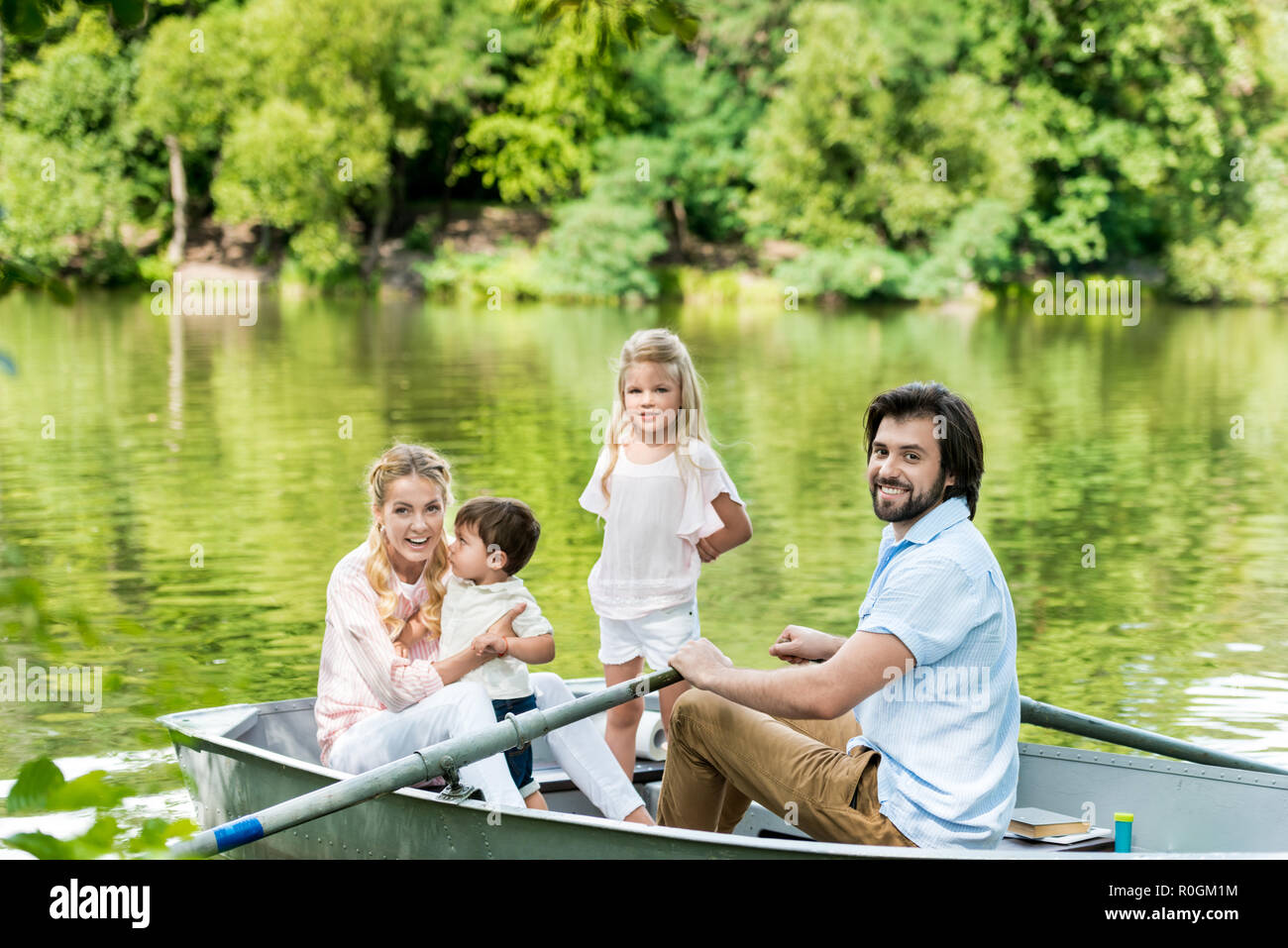 happy young family riding boat on lake at park and looking at camera ...