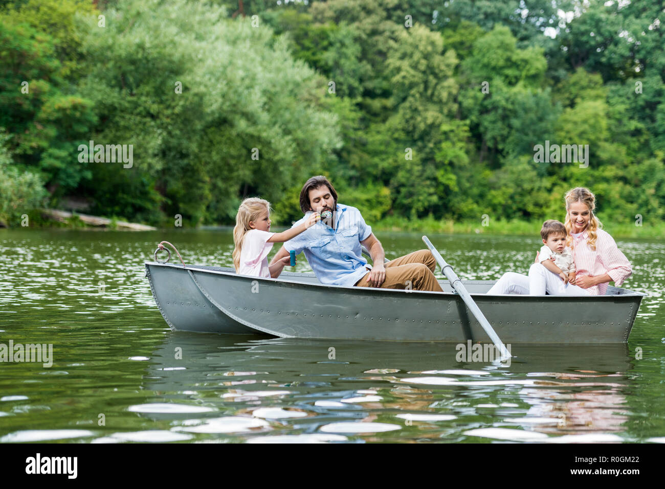 beautiful young family spending time together in boat on lake at park ...
