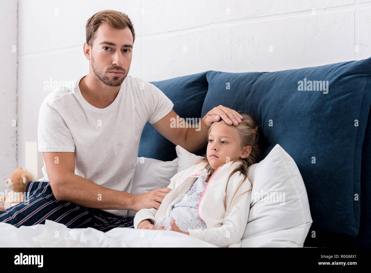 father checking daughters temperature with hand while she lying in bed ...