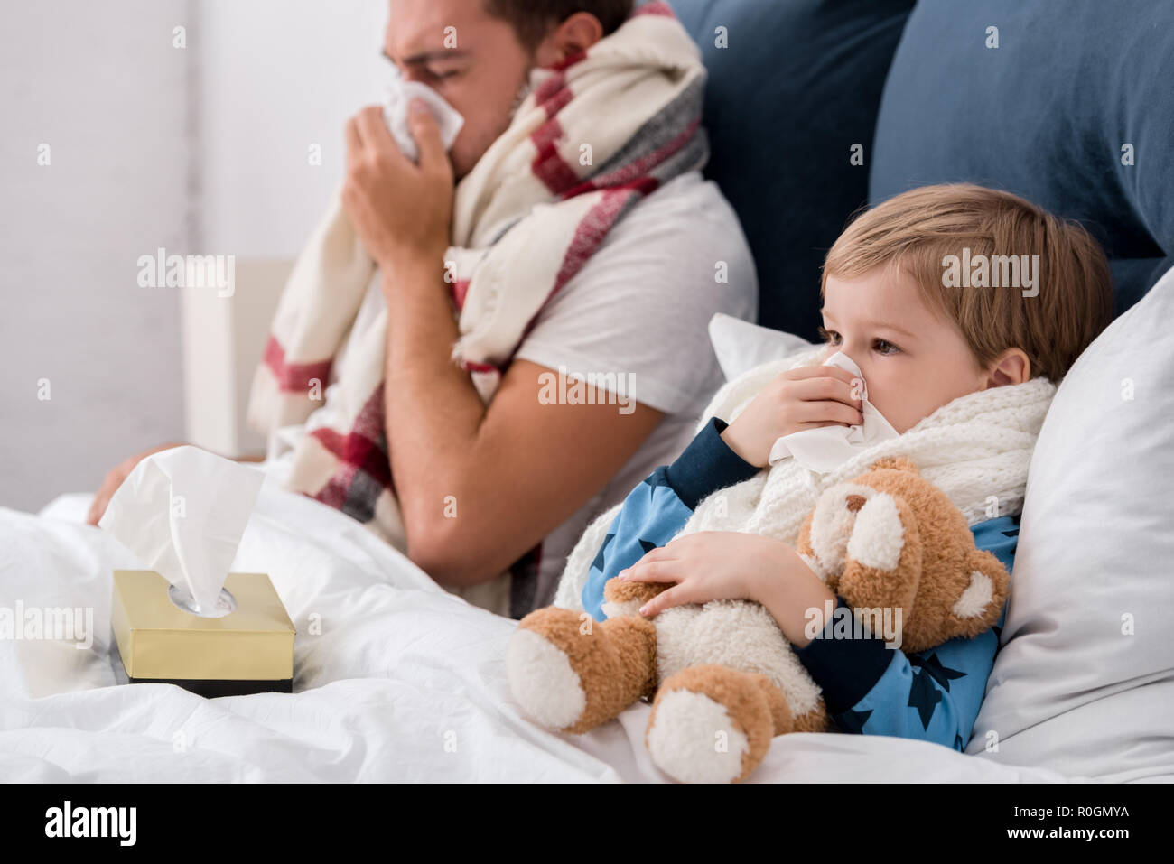 sick father and son blowing noses with paper napkins while lying in bed ...