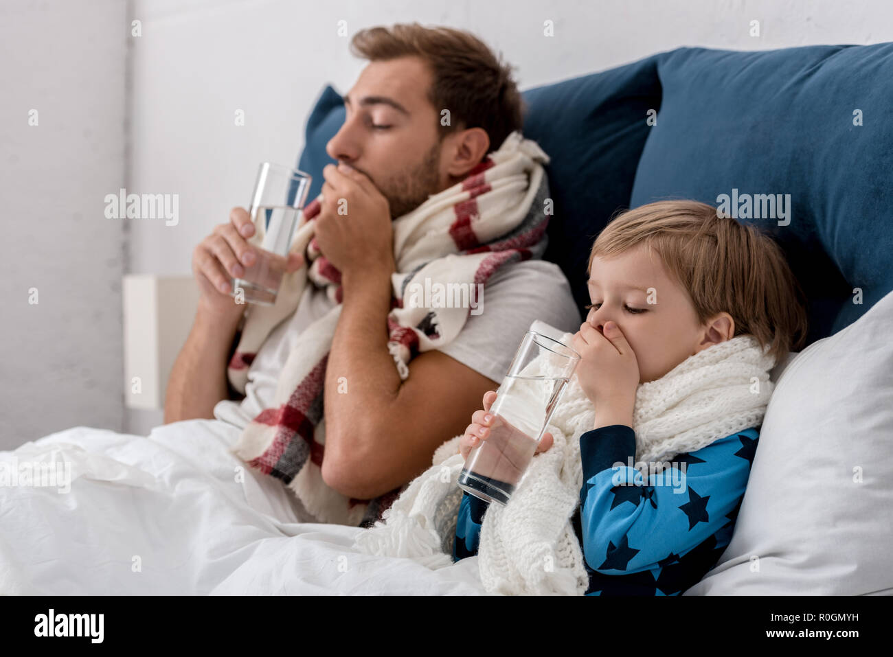 sick father and son with glasses of water taking pills while sitting in ...