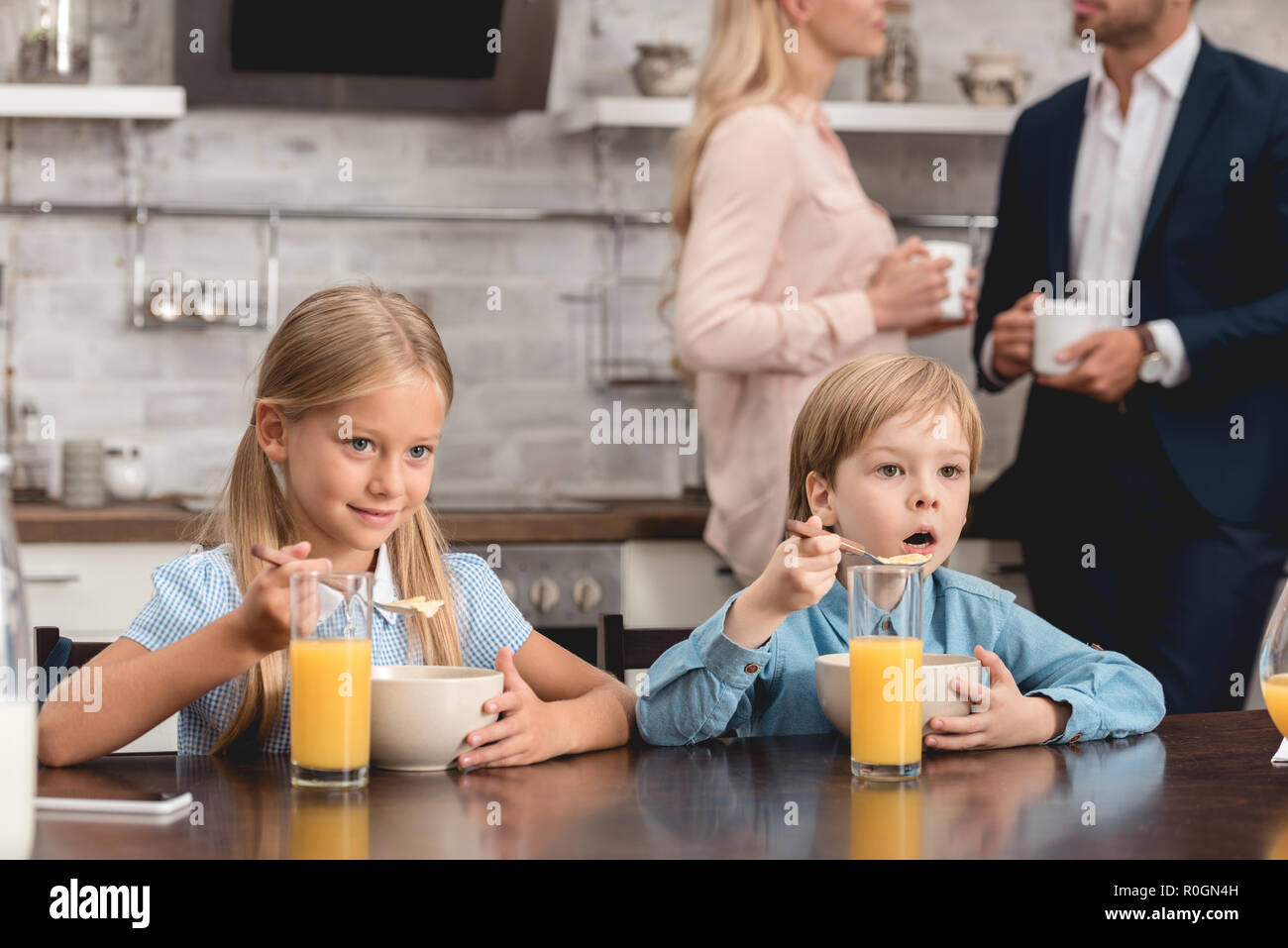 cute little kids having breakfast together at kitchen while parents ...
