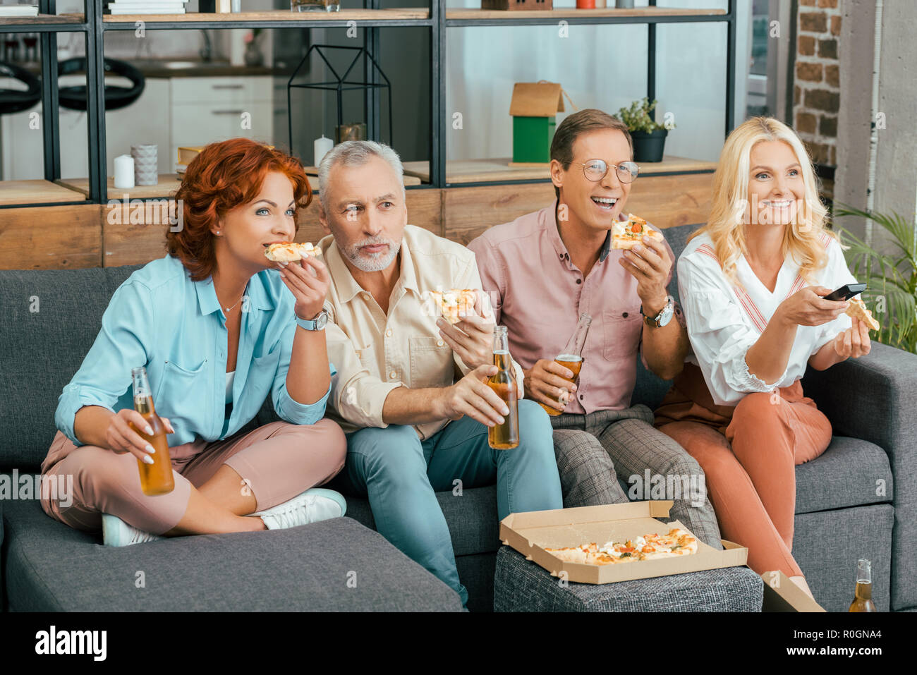 happy mature friends eating pizza and drinking beer while using remote ...