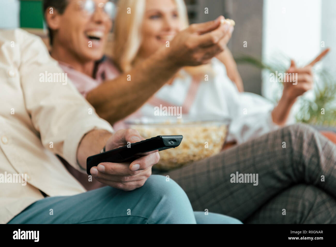 cropped shot of mature friends using remote controller and eating ...