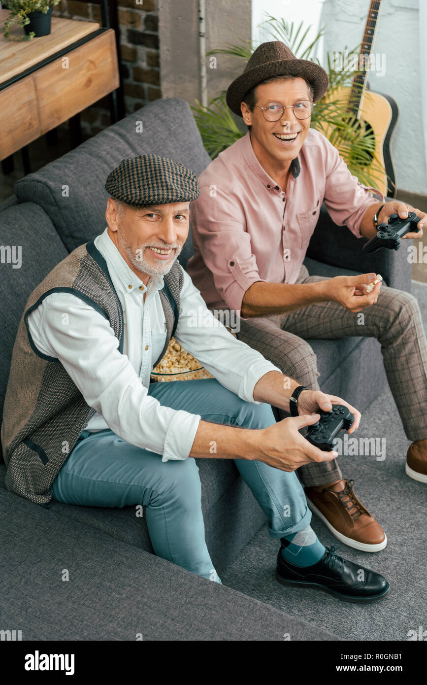 happy mature men playing with joysticks and smiling at camera, high ...