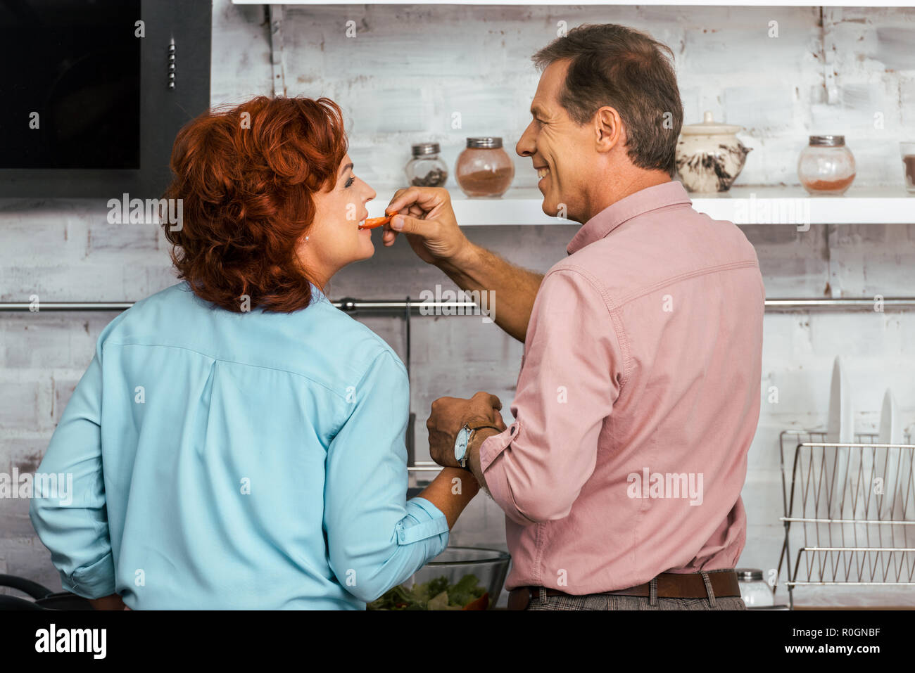 back view of smiling man feeding beautiful mature woman while standing ...