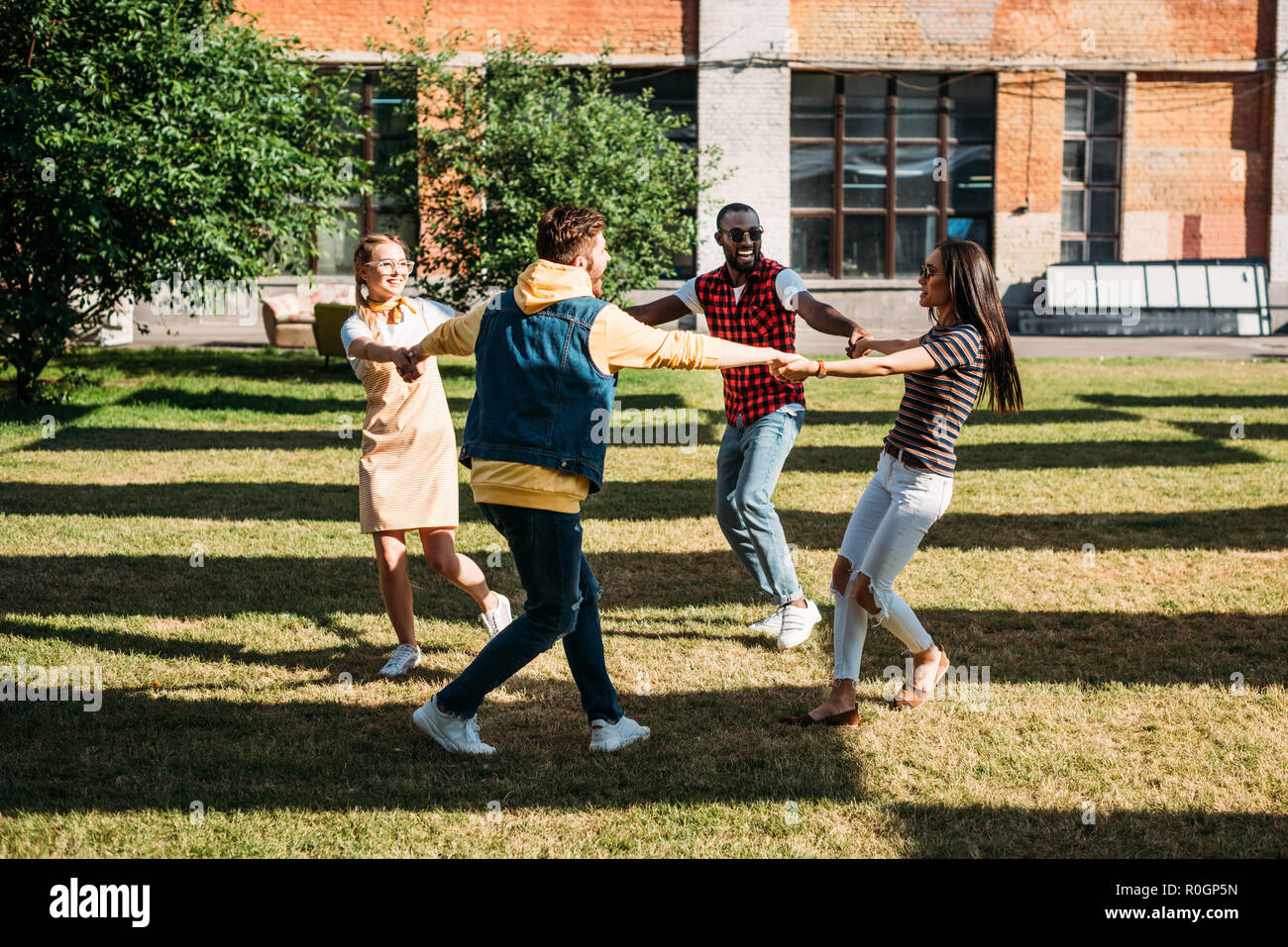 multicultural young friends holding hands while having fun together on ...