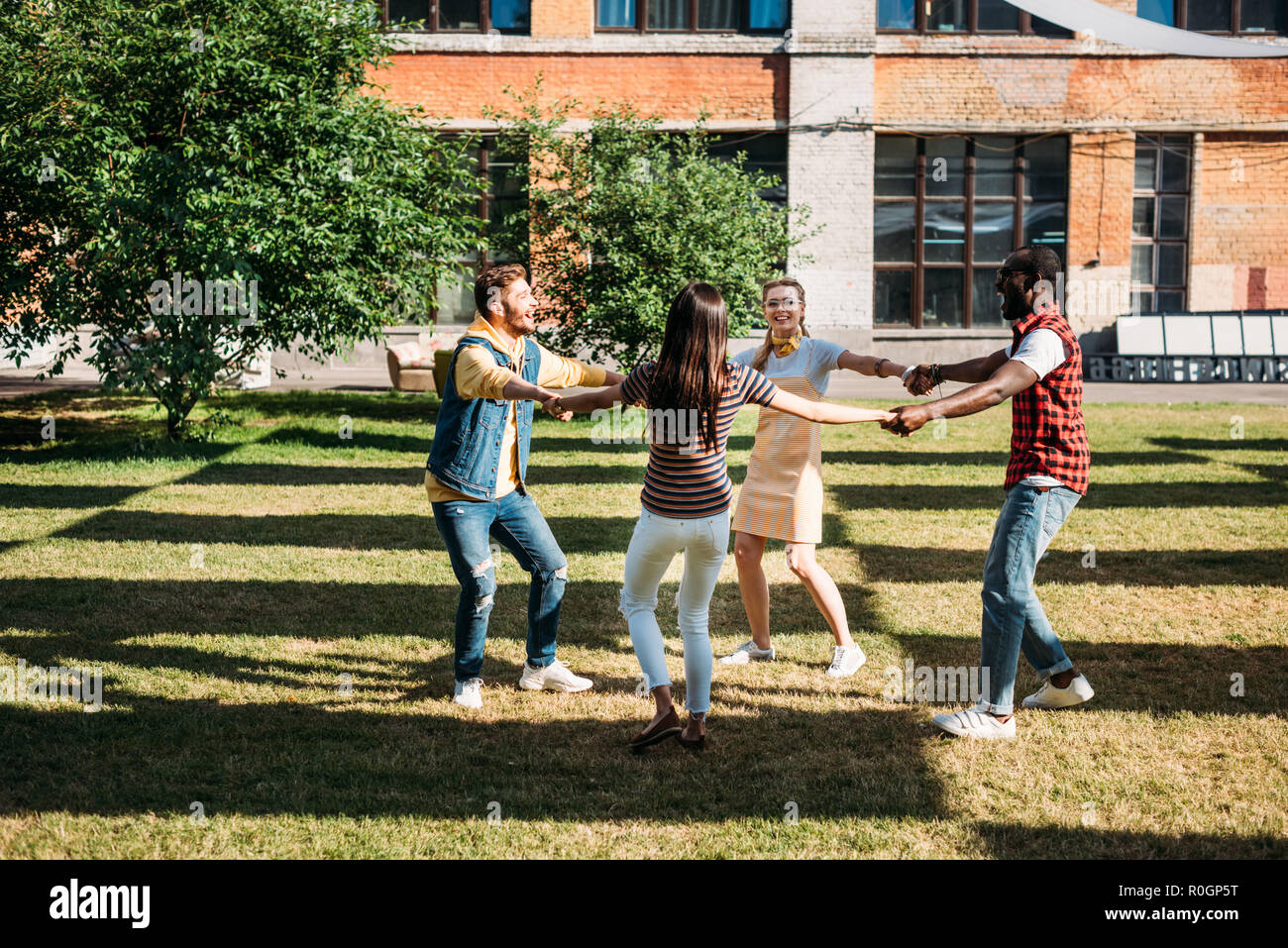 multicultural young friends holding hands while having fun together on ...