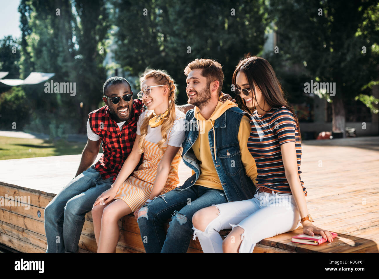 multicultural cheerful couples sitting on wooden parapet together Stock Photo - Alamy