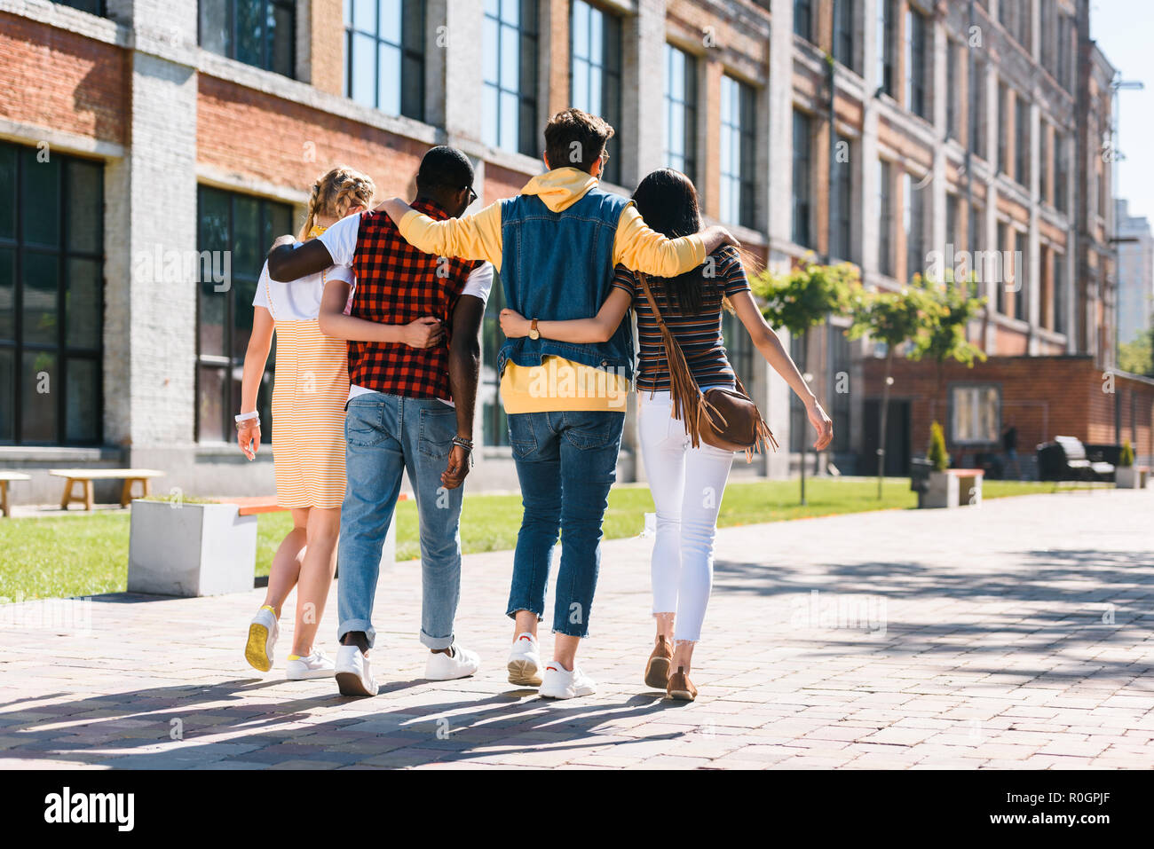 back view of multicultural group of friends hugging while walking on ...