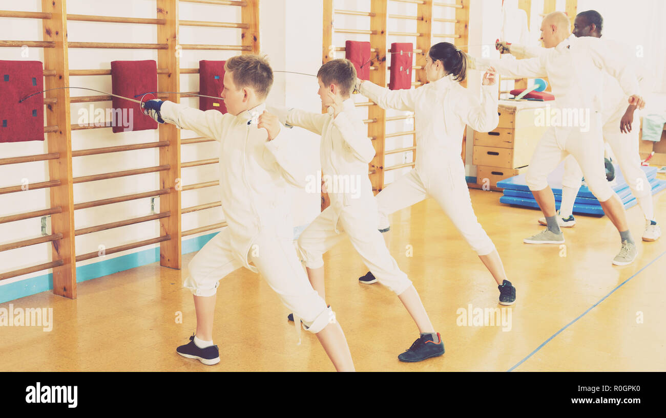 Kids with adults practicing effective techniques of fencing in gym ...
