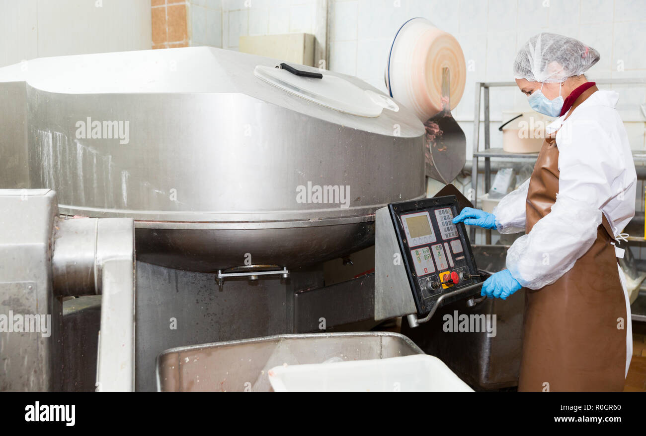 Woman worker of sausage factory pushing buttons on control panel of ...