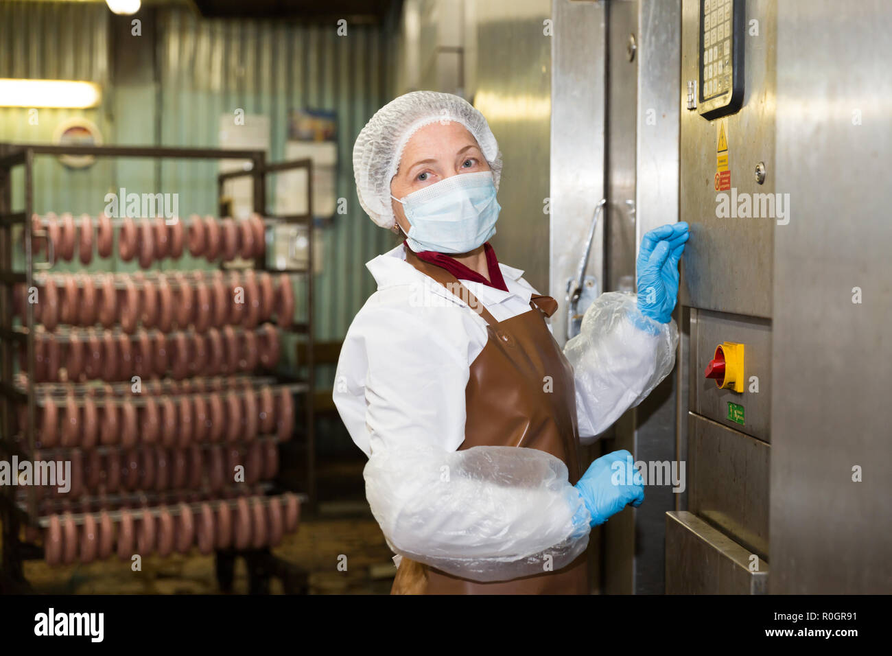 Female worker operating industrial smoking furnace for sausages on meat ...