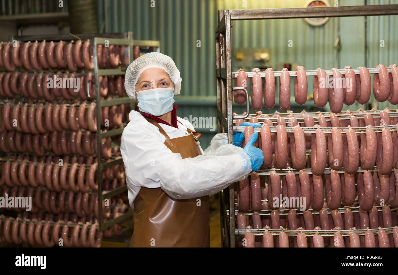 Female worker carrying raw sausages on racks in storage room at meat ...
