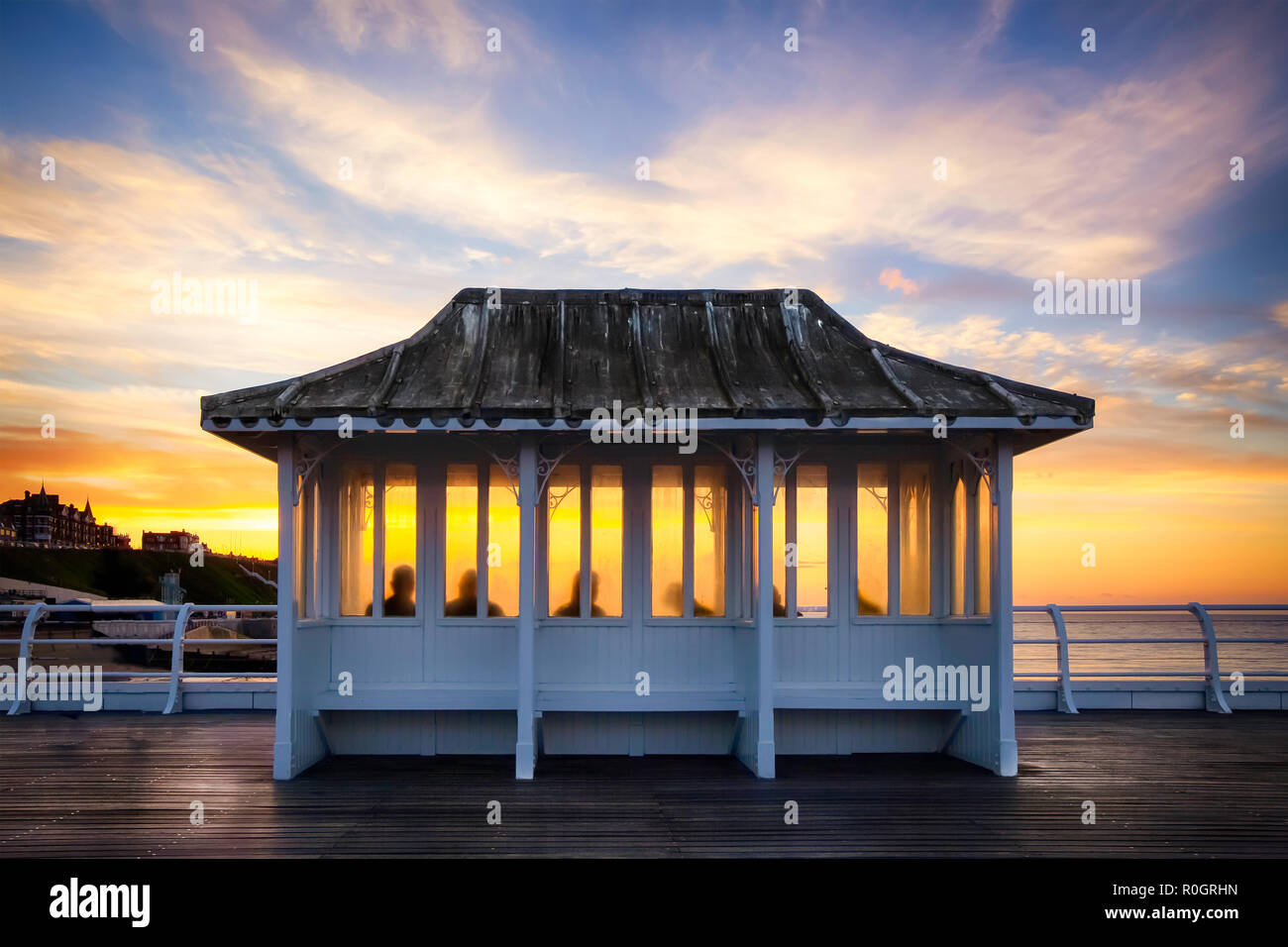 Historic victorian pier shelter at sunset with people in silhouette sat ...